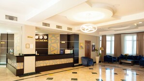 Uma área de recepção de hotel com balcão, relógio, espaço de estar com sofás e um grande candelabro.