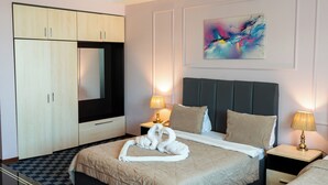 Quarto de hotel com chão quadriculado, cama com toalha em formato de coração, duas mesas de cabeceira com abajures, um guarda-roupa e um quadro na parede.
