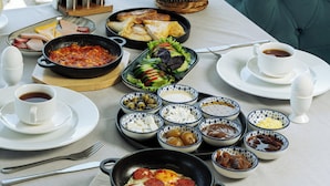 Uma mesa de jantar com diversos pratos, uma cesta de pão e vista para árvores pela janela.