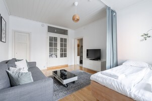 Uma sala de estar moderna com um sofá cinza, uma mesa de centro, uma cama e uma televisão.