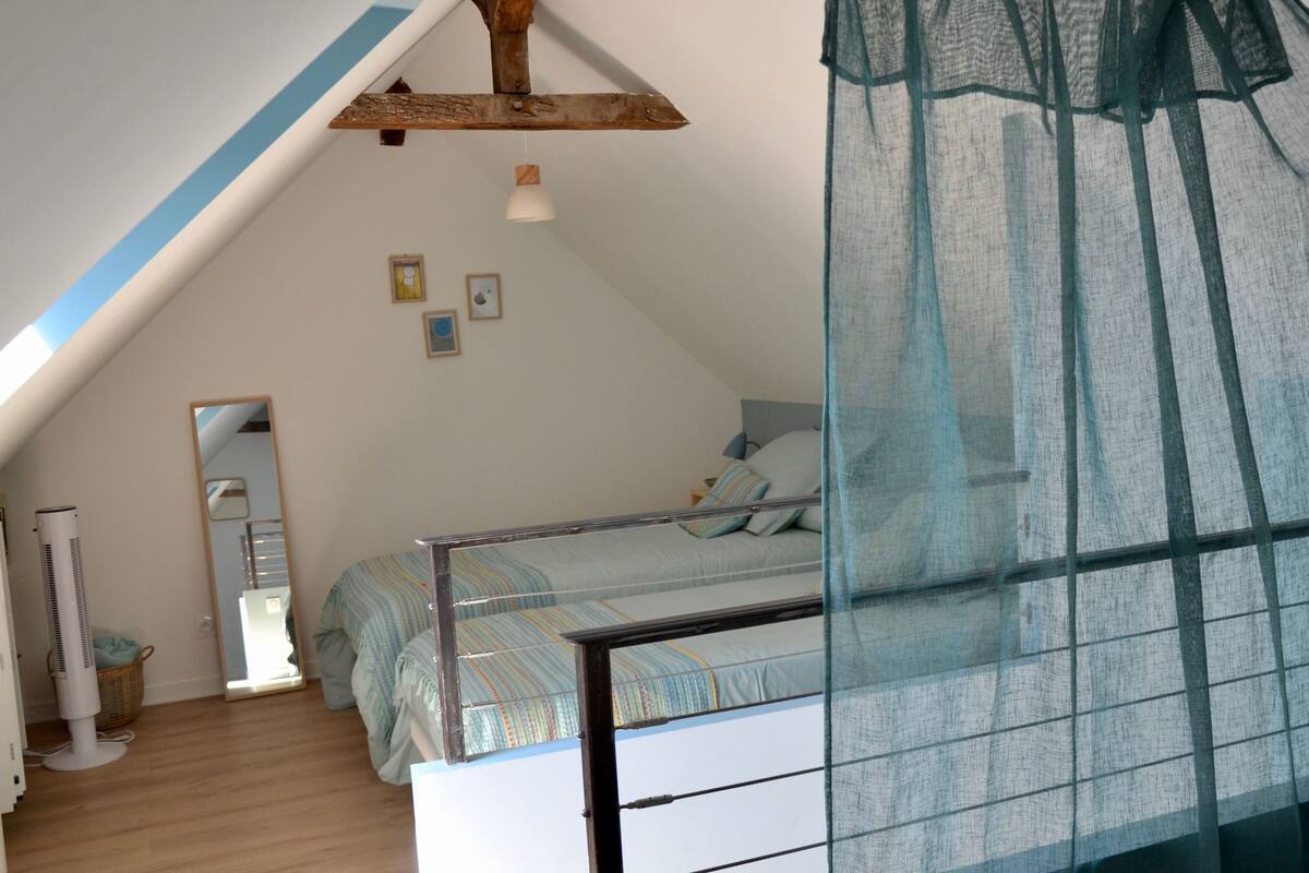 Quarto com cama beliche, ventilador de teto, espelho e janela com cortinas leves.