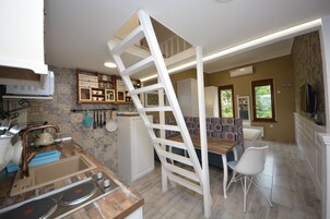 Cozinha com bancada de madeira, pia e escada branca. Há uma área de refeições com mesa e cadeiras.