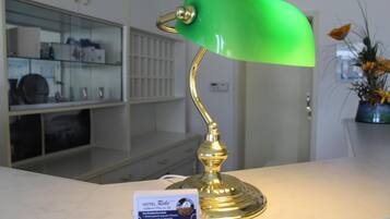 Luminária de mesa verde com base em latão sobre um balcão de recepção de hotel.