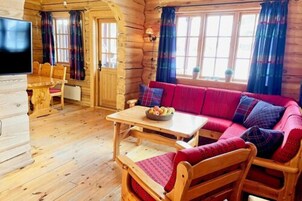 Interior acolhedor de uma cabana com uma mesa de jantar de madeira, um sofá e uma televisão.