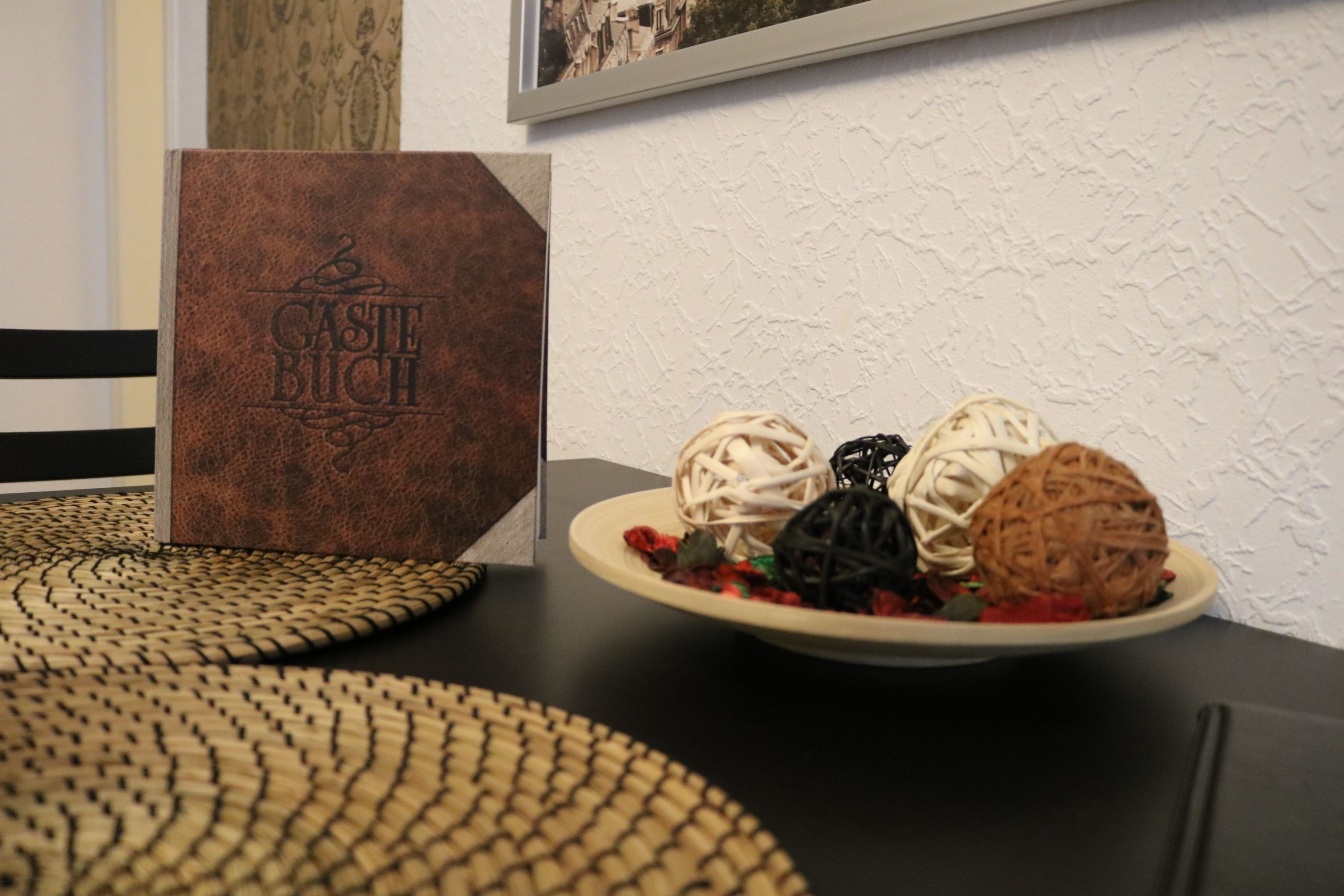 Uma mesa com um prato de bolas decorativas, uma caixa marrom com a inscrição 'Caste Buch' e jogos americanos trançados.