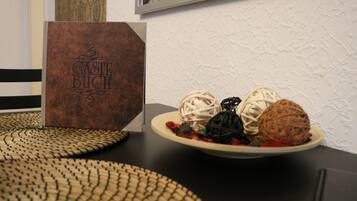 Uma mesa com um prato de bolas decorativas, uma caixa marrom com a inscrição 'Caste Buch' e jogos americanos trançados.