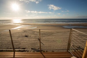 Vista da praia a partir de um deck de madeira com guarda-corpo de metal.