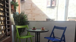 Uma pequena varanda com uma mesa redonda e duas cadeiras, uma verde e outra azul.