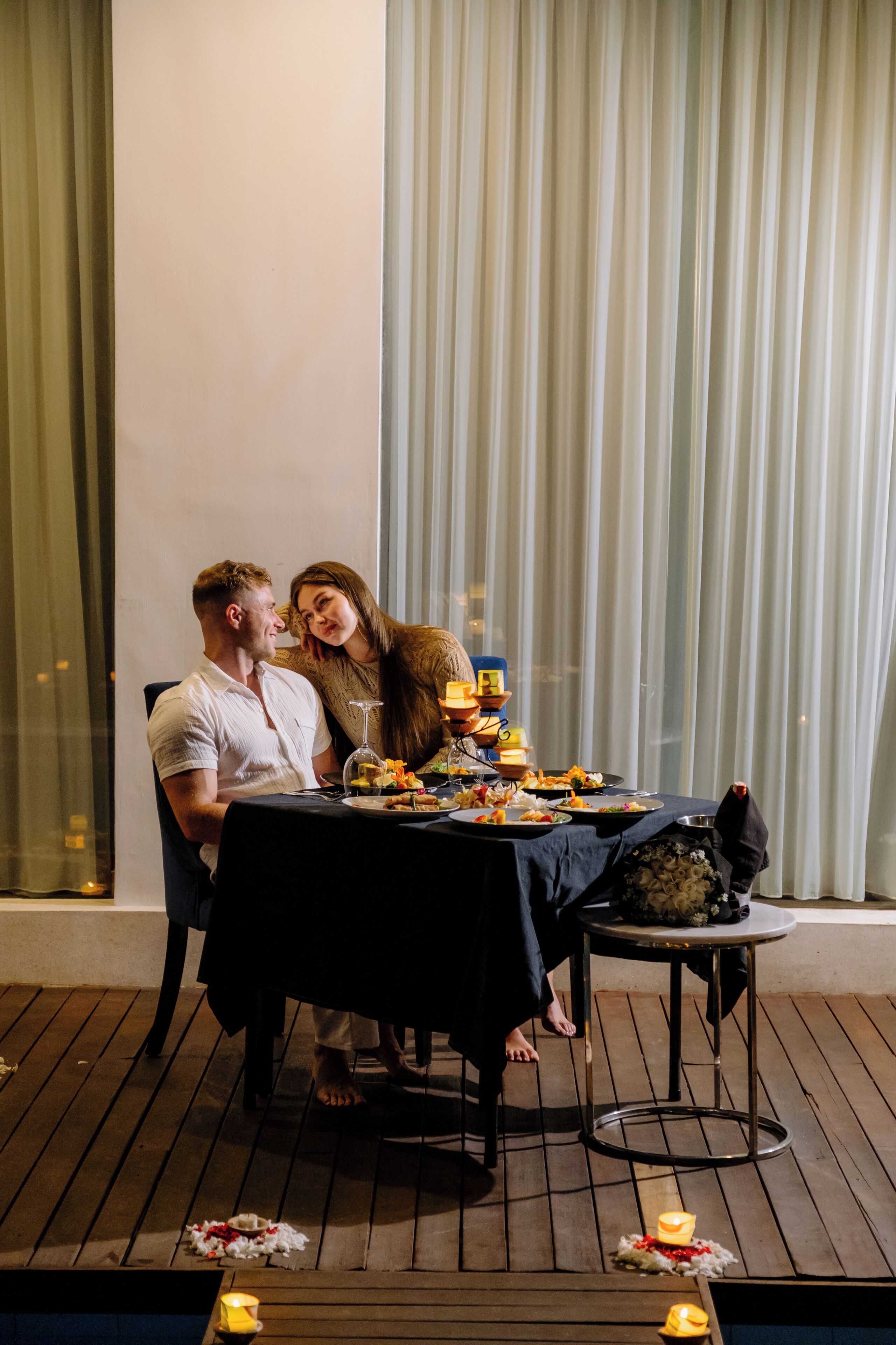 Um casal jantando em mesa ao ar livre, com vista para o horizonte da cidade.