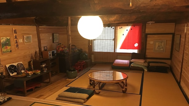 Um quarto japonês tradicional com tatames, uma mesa baixa, almofadas e diversos objetos decorativos.