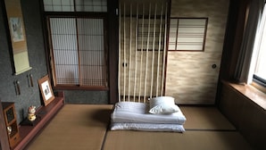 Um quarto com esteiras de tatame, uma cama futon, um biombos shoji e uma pequena prateleira com uma estatueta de gato.