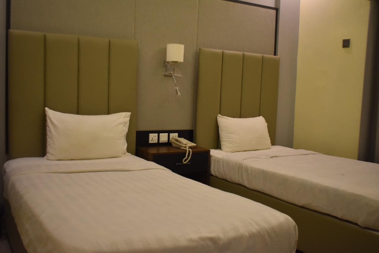 Quarto de hotel com duas camas de solteiro, um telefone ao lado da cama e uma luminária na parede.