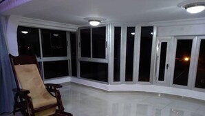 Um quarto amplo, com grandes janelas, uma cadeira de madeira e piso de azulejos.