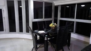 Uma área de refeições com mesa de vidro, cadeiras pretas e um vaso de flores.