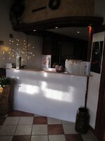 Uma área de recepção com piso de azulejos, balcão de atendimento, um vaso com iluminação e um cartaz na parede.