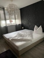 Quarto com uma cama grande, parede escura e um candelabro.