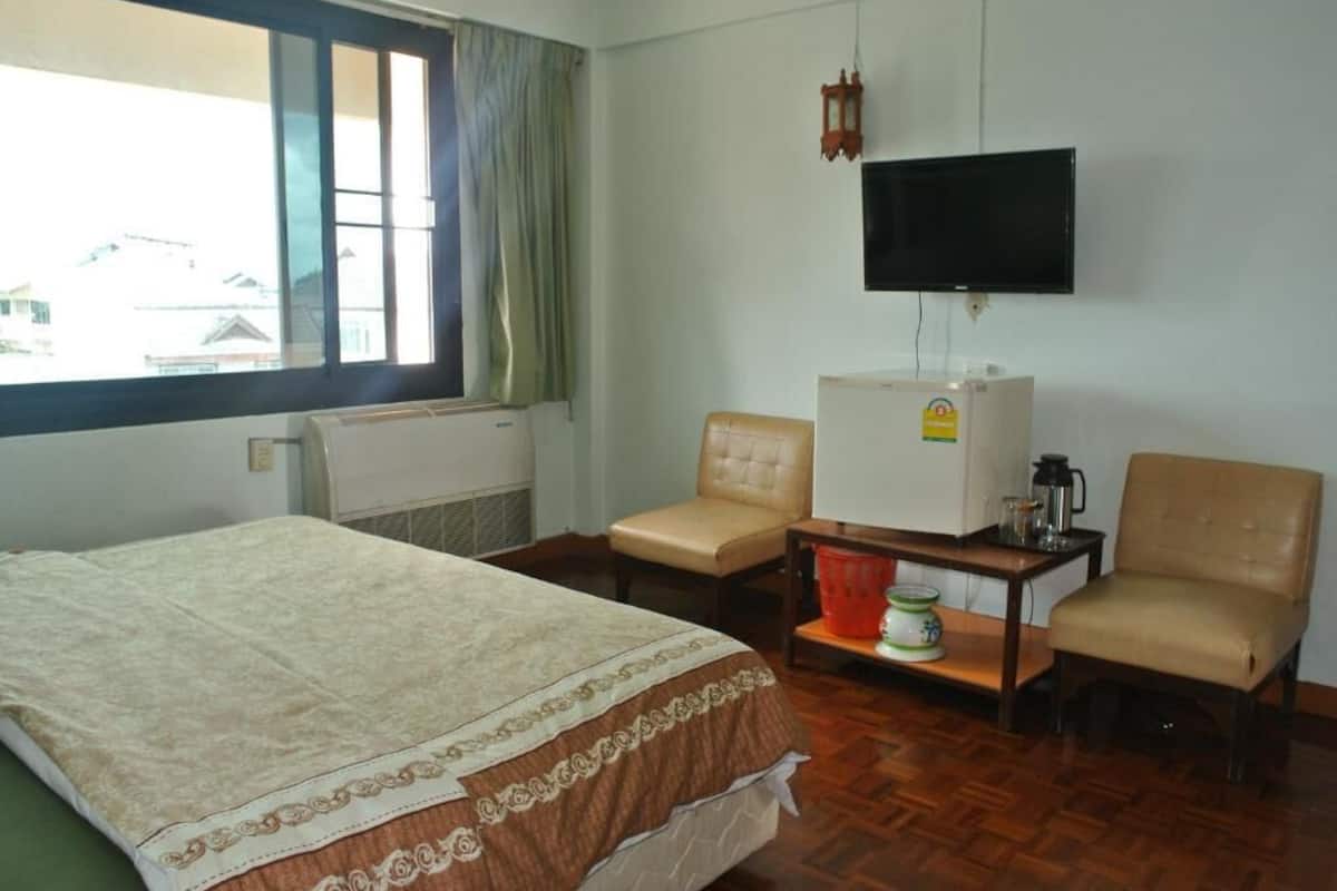 Quarto de hotel com cama, duas cadeiras, televisão, pequena mesa com cafeteira e janela com cortinas.