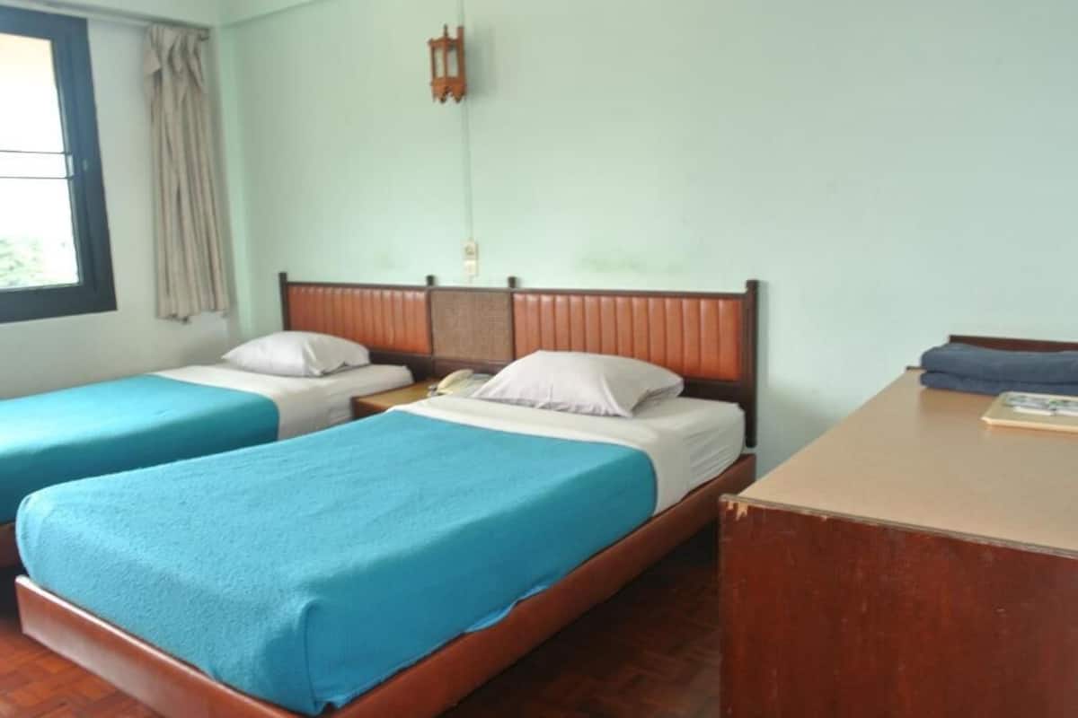 Quarto com duas camas, uma escrivaninha de madeira, uma janela com cortinas e um abajur fixado na parede.