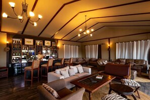 Uma sala de estar ampla, com bar, diversas opções de assento e um lustre.