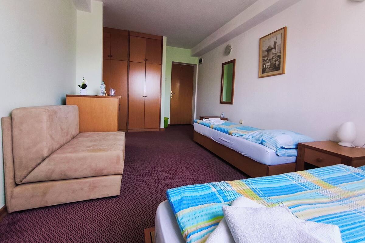 Quarto de hotel com cama, sofá, escrivaninha, guarda-roupa e espelho.