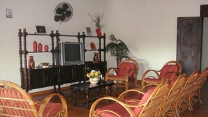 Uma sala de estar com móveis de vime, uma televisão e um ventilador.
