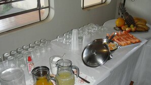 Uma mesa de buffet com copos de plástico transparente, jarras de bebidas e uma variedade de frutas e legumes.