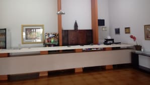 Uma área de recepção com balcão, obras de arte emolduradas, uma pequena estátua e um vaso com planta.