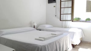 Quarto de hotel com duas camas, uma mesa, uma luminária e uma janela com cortinas.