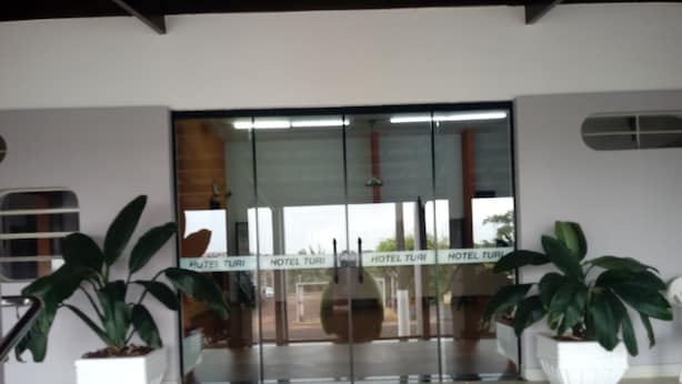 Entrada de hotel com portas de vidro e plantas em vasos de ambos os lados.