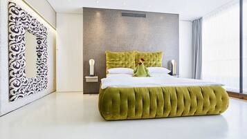 Quarto moderno com uma cama grande, um detalhe decorativo na parede e uma janela ampla com cortinas.