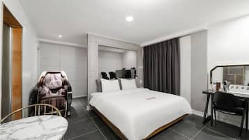 Quarto de hotel moderno com uma cama grande, uma cadeira de massagem, uma mesa com cadeira e um banheiro com chuveiro e vaso sanitário.
