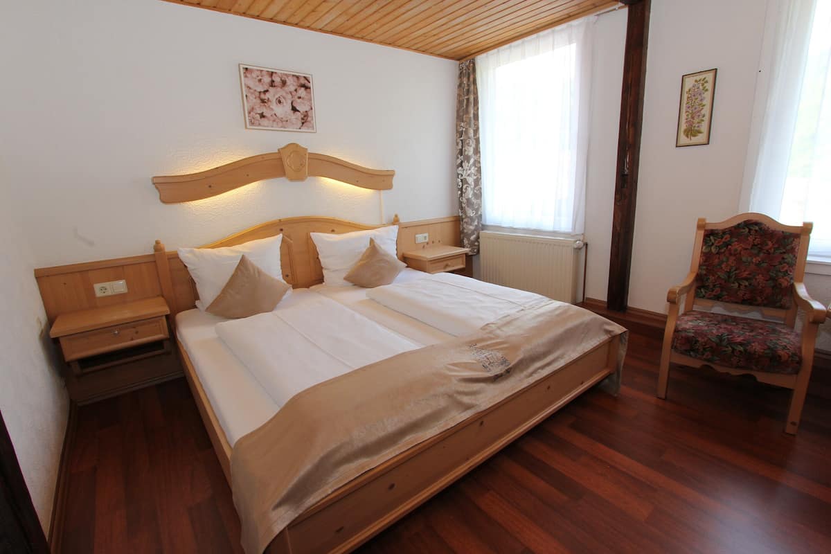 Quarto com cama de madeira, mesas de cabeceira, uma cadeira e arte floral nas paredes.