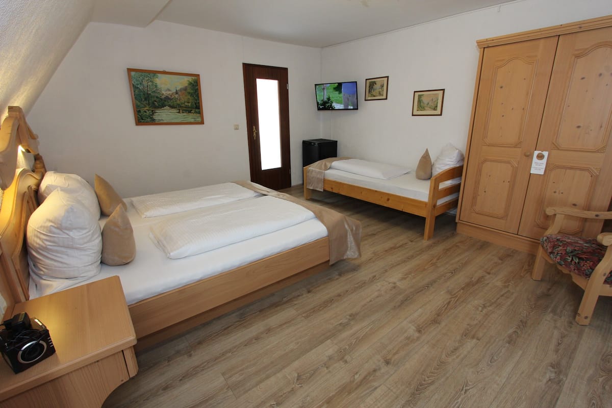 Quarto com duas camas de solteiro, um guarda-roupa, uma televisão e uma câmara num criado-mudo.
