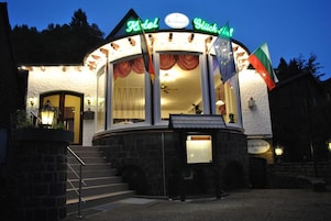 Um hotel com fachada curva, uma placa com a inscrição "Hotel Glück" e várias bandeiras.