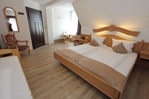 Quarto com uma cama grande, cabeceira de madeira, uma cadeira, uma mesinha e uma porta.