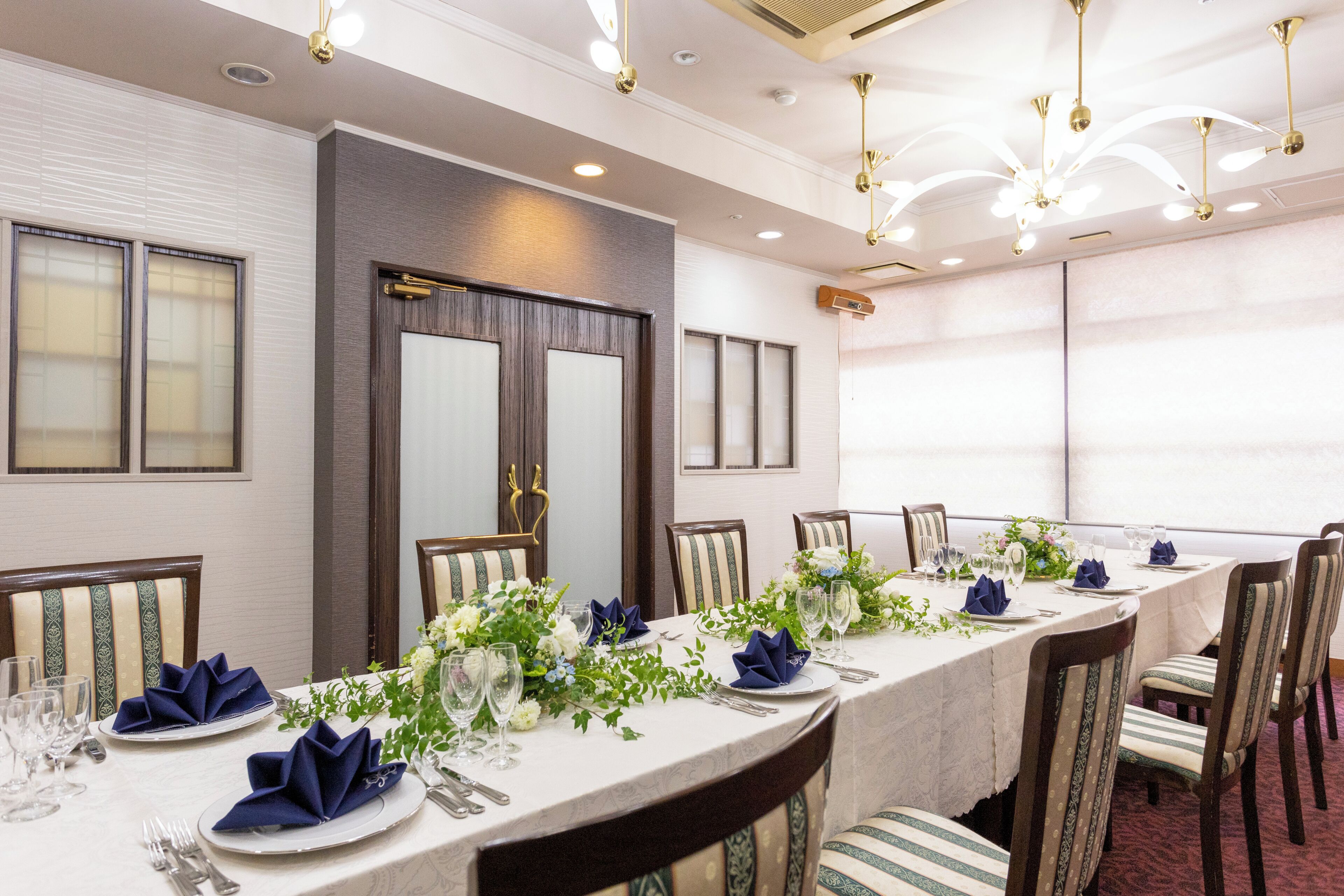 Uma longa mesa de jantar com cadeiras, posta para uma refeição formal, num quarto bem iluminado com design moderno no teto.