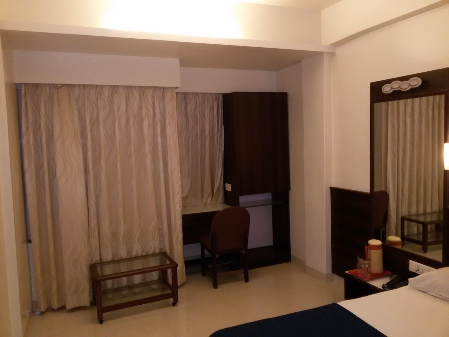 Quarto de hotel com cama, escrivaninha, cadeira, mesinha e espelho.