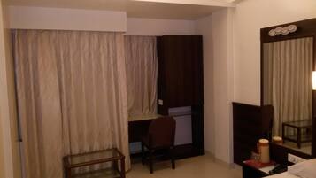 Quarto de hotel com cama, escrivaninha, cadeira, mesinha e espelho.