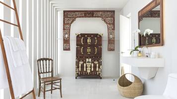 Casa de banho com cadeira de madeira, lavatório branco, espelho e porta decorativa.