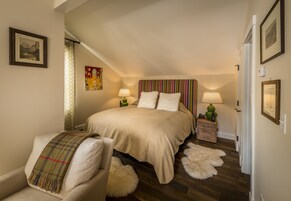 Quarto com cama, duas mesas de cabeceira, uma cadeira, tapete de pele e um quadro na parede.