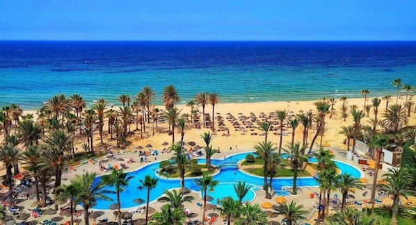 Um resort com várias piscinas, palmeiras e uma praia.