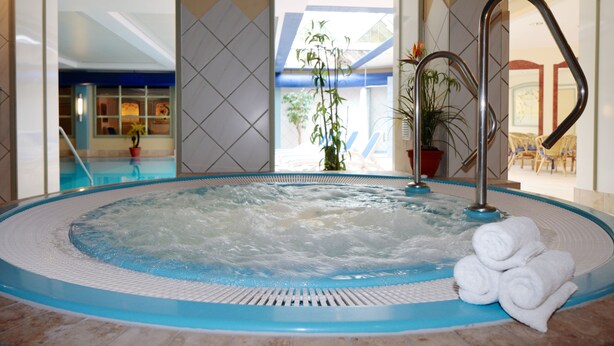 Uma banheira de hidromassagem com vista para uma piscina e área de estar interna.