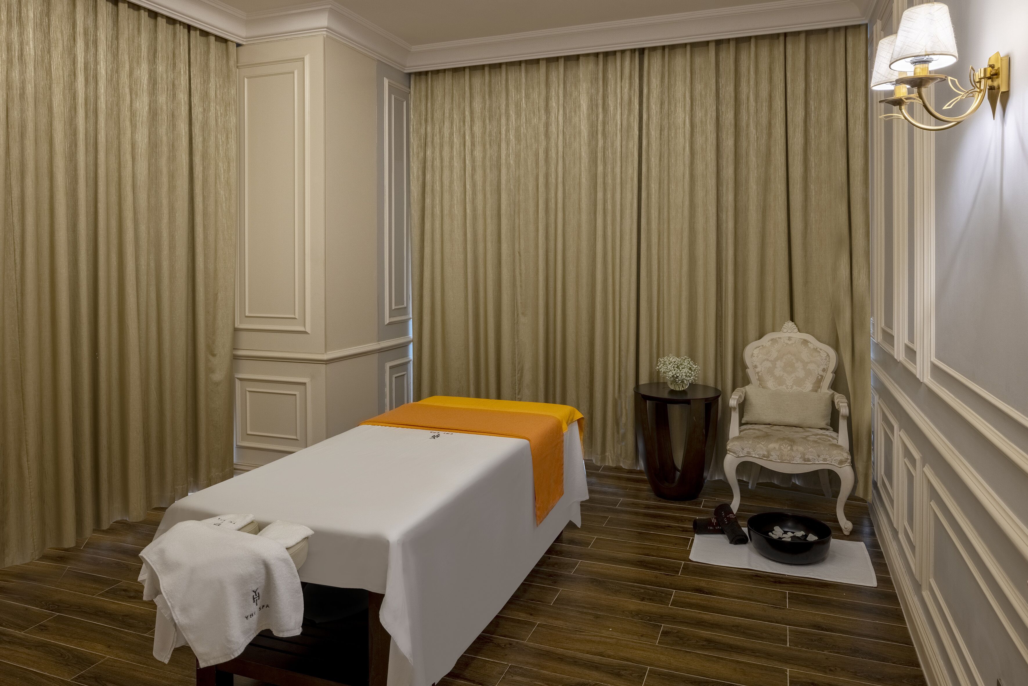 Um quarto com mesa de massagem, uma cadeira, uma mesinha com uma tigela e um abajur.