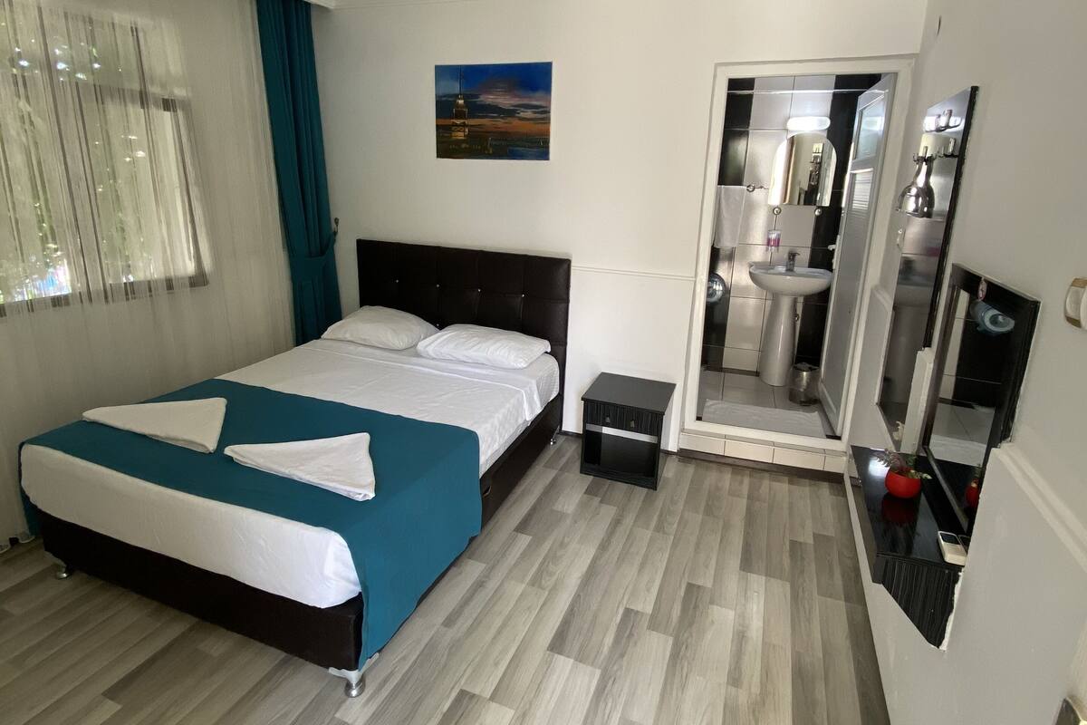 Quarto de hotel com cama, mesa de cabeceira e banheiro com espelho e pia.