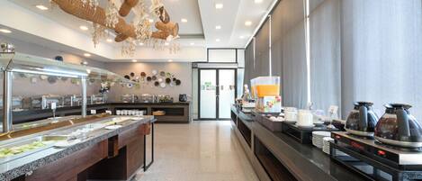 Uma mesa de buffet moderna com diversos pontos de comida, uma máquina de café e um teto decorativo.