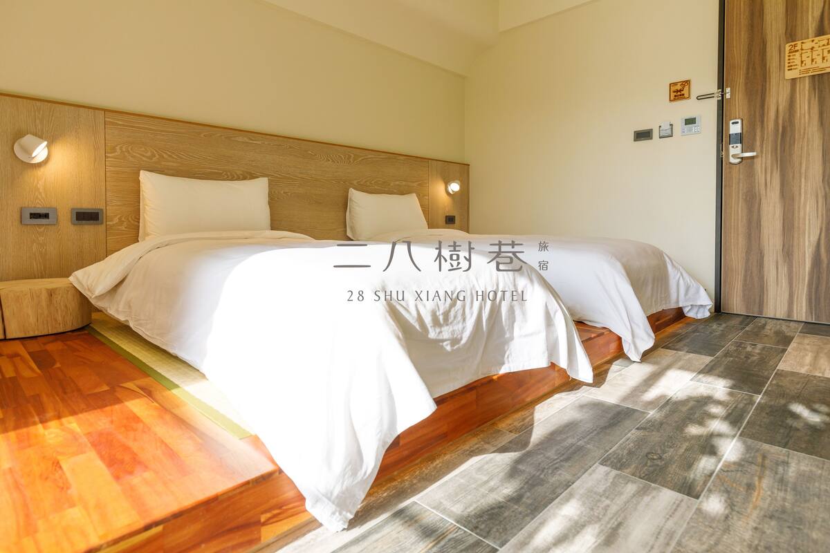 Quarto de hotel com cabeceira de madeira, cama com roupa de cama branca e chão em azulejos.