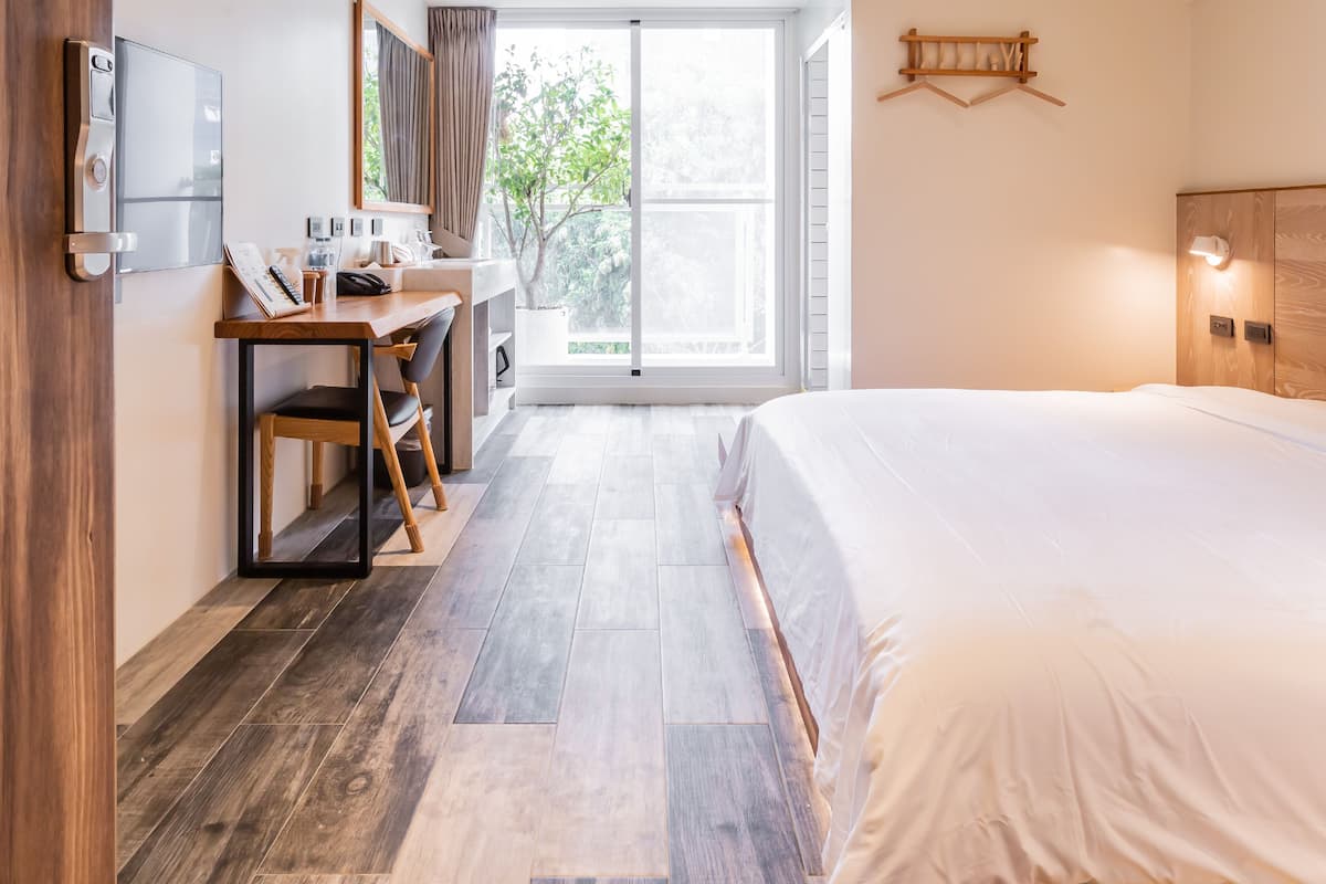 Quarto de hotel com uma cama, uma escrivaninha com cadeira, televisão e janela com cortinas.