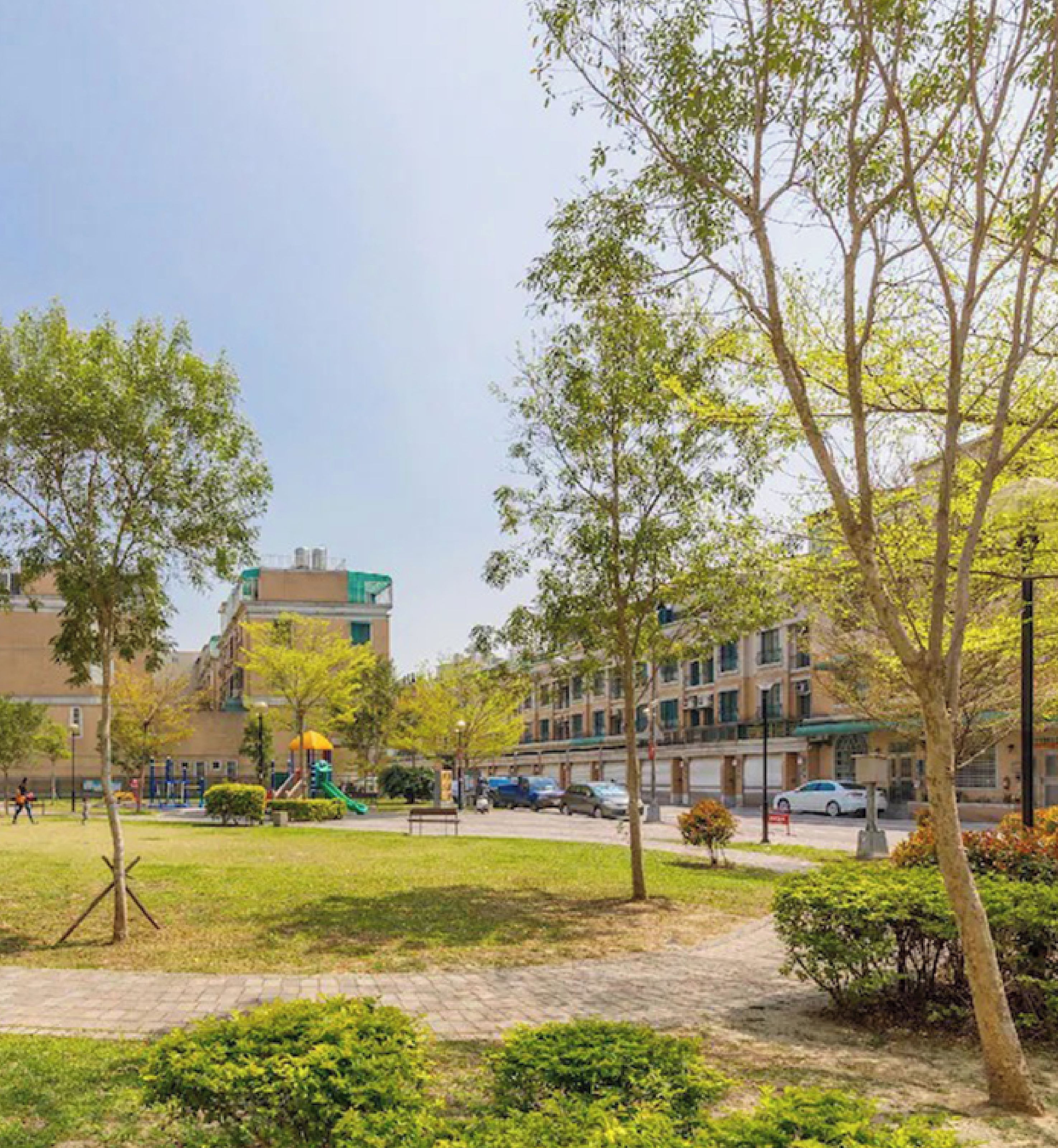 Uma área de parque com parquinho, bancos e um caminho pavimentado.