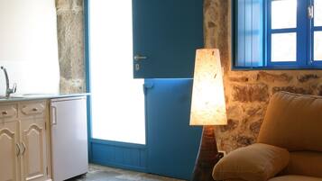 Um quarto com parede de pedra, porta azul, armário branco, luminária e sofá bege.