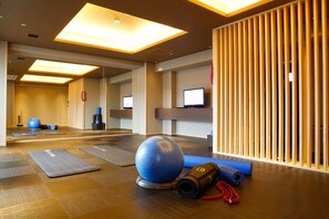 Uma academia espaçosa com colchonetes de exercício, uma grande bola de ginástica e tapetes de yoga no chão.